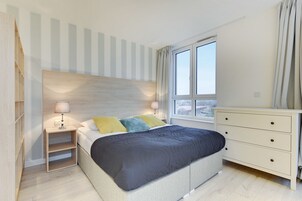 Quarto moderno com uma cama grande, mesas de cabeceira, cômoda e janela com cortinas.