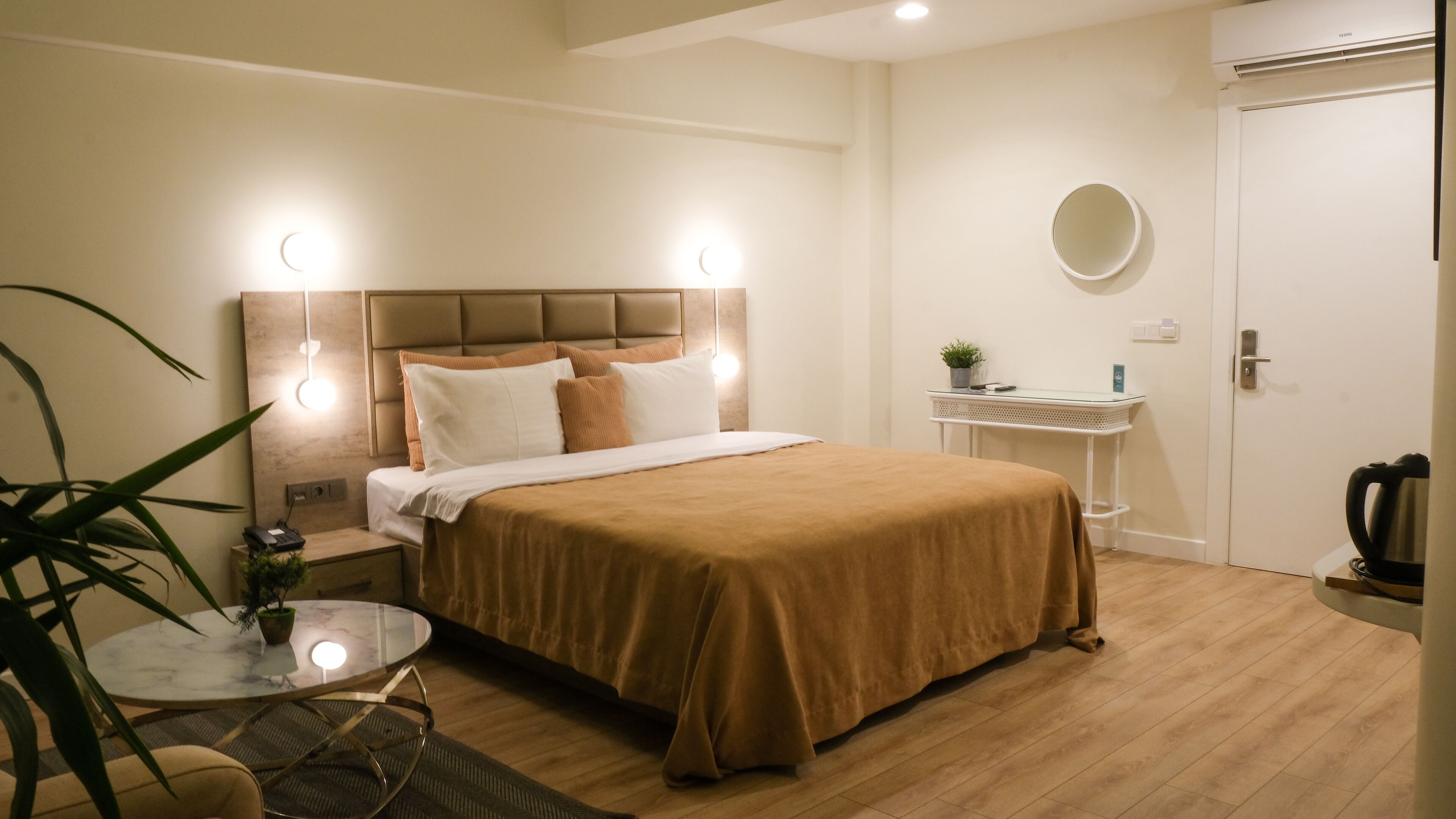 Quarto de hotel com cama, mesa de cabeceira, abajur e um pequeno espelho redondo na parede.