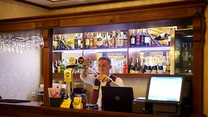 Uma área de bar com um barman, um computador e diversas garrafas de bebidas alcoólicas.