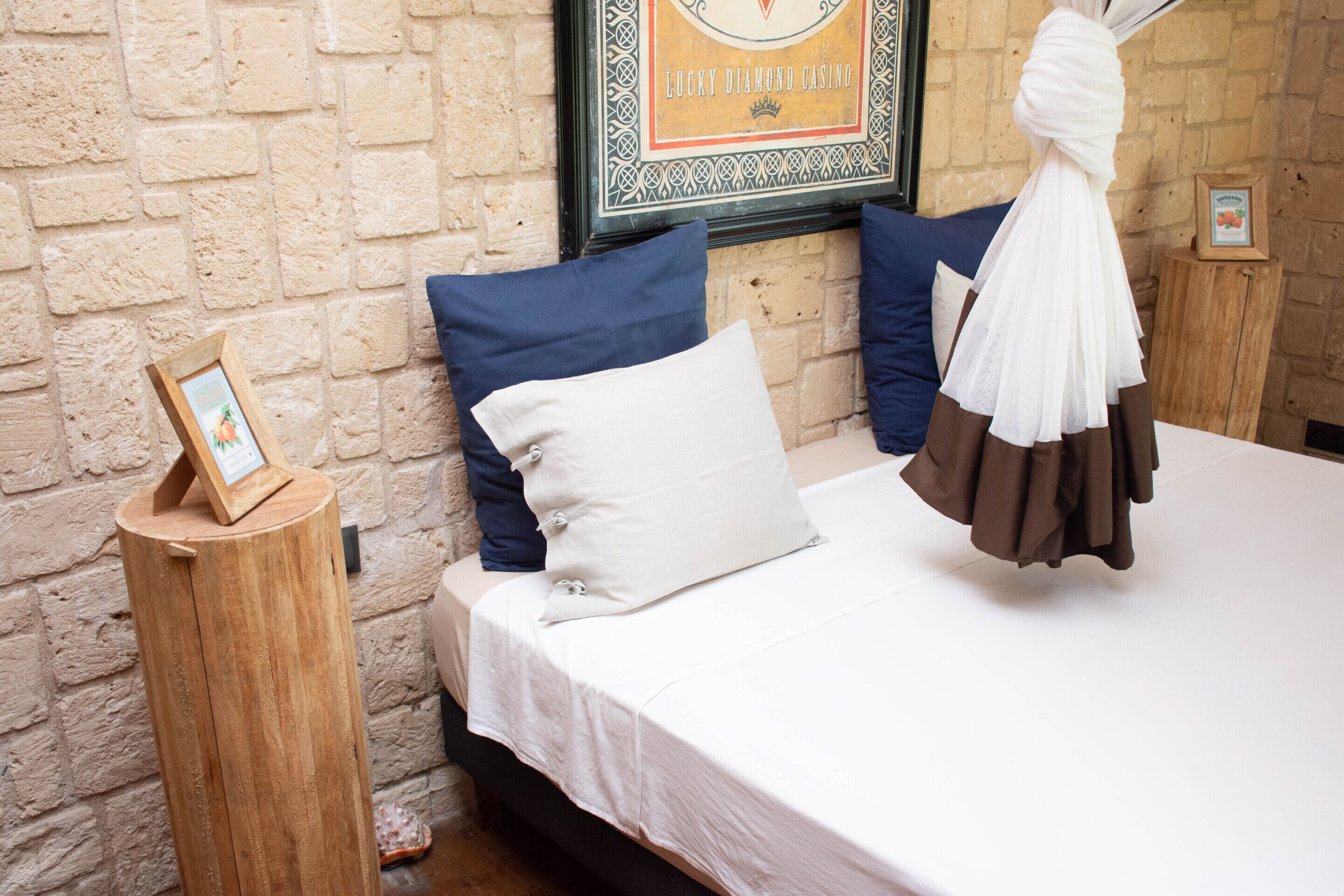 Cama bem arrumada com manta branca e marrom, almofadas azuis e um quadro numa mesa de cabeceira de madeira.