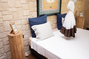 Cama bem arrumada com manta branca e marrom, almofadas azuis e um quadro numa mesa de cabeceira de madeira.