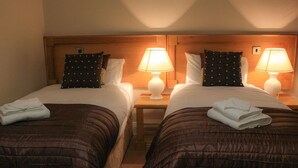 Quarto de hotel com duas camas, cada uma com cabeceira de madeira, mesa de cabeceira e luminária.
