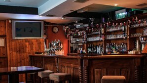 Uma área de bar com balcões de madeira, banquetas e prateleiras cheias de garrafas.