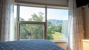 Quarto com uma cama grande, janela com cortinas e vista para uma paisagem verde.