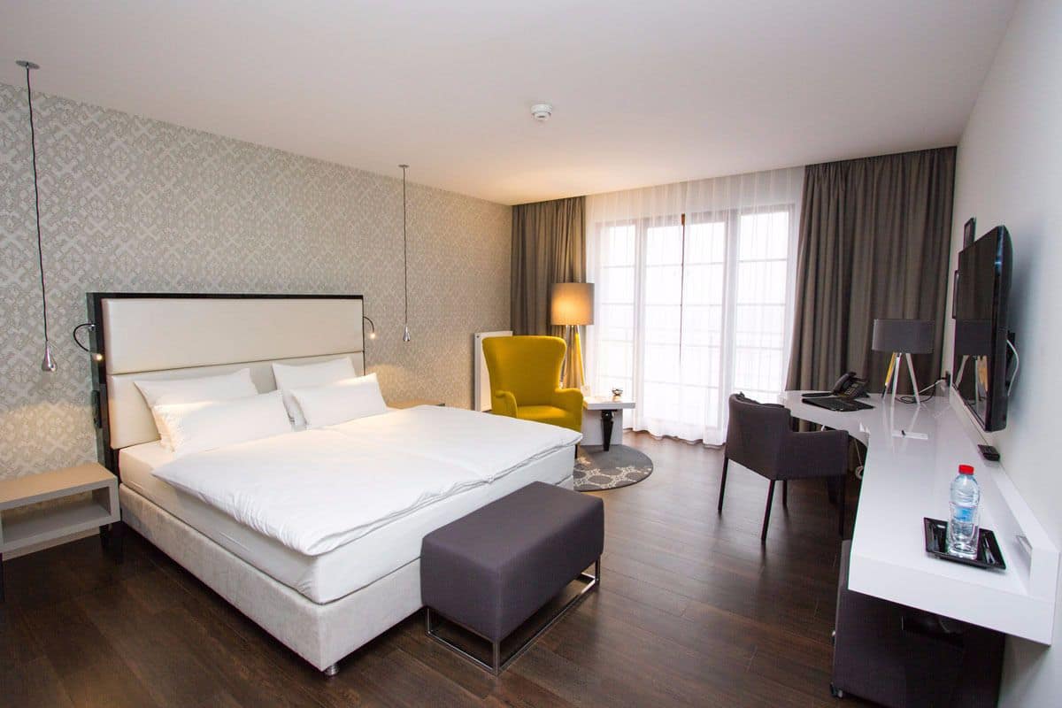 Quarto de hotel com uma cama grande, uma mesa com cadeira, uma televisão e uma luminária.