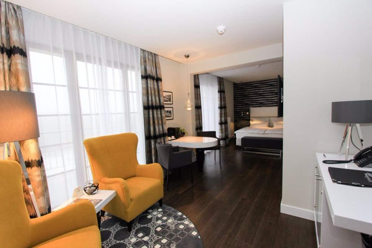 Quarto de hotel com cama, escrivaninha, cadeira e área de refeições.