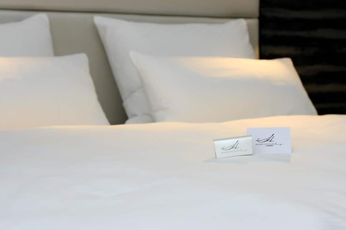 Cama bem arrumada com lençóis brancos e duas etiquetas com nomes sobre ela.