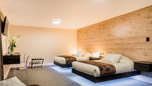 Quarto moderno com duas camas, uma parede de destaque em madeira, uma escrivaninha pequena e uma cadeira.