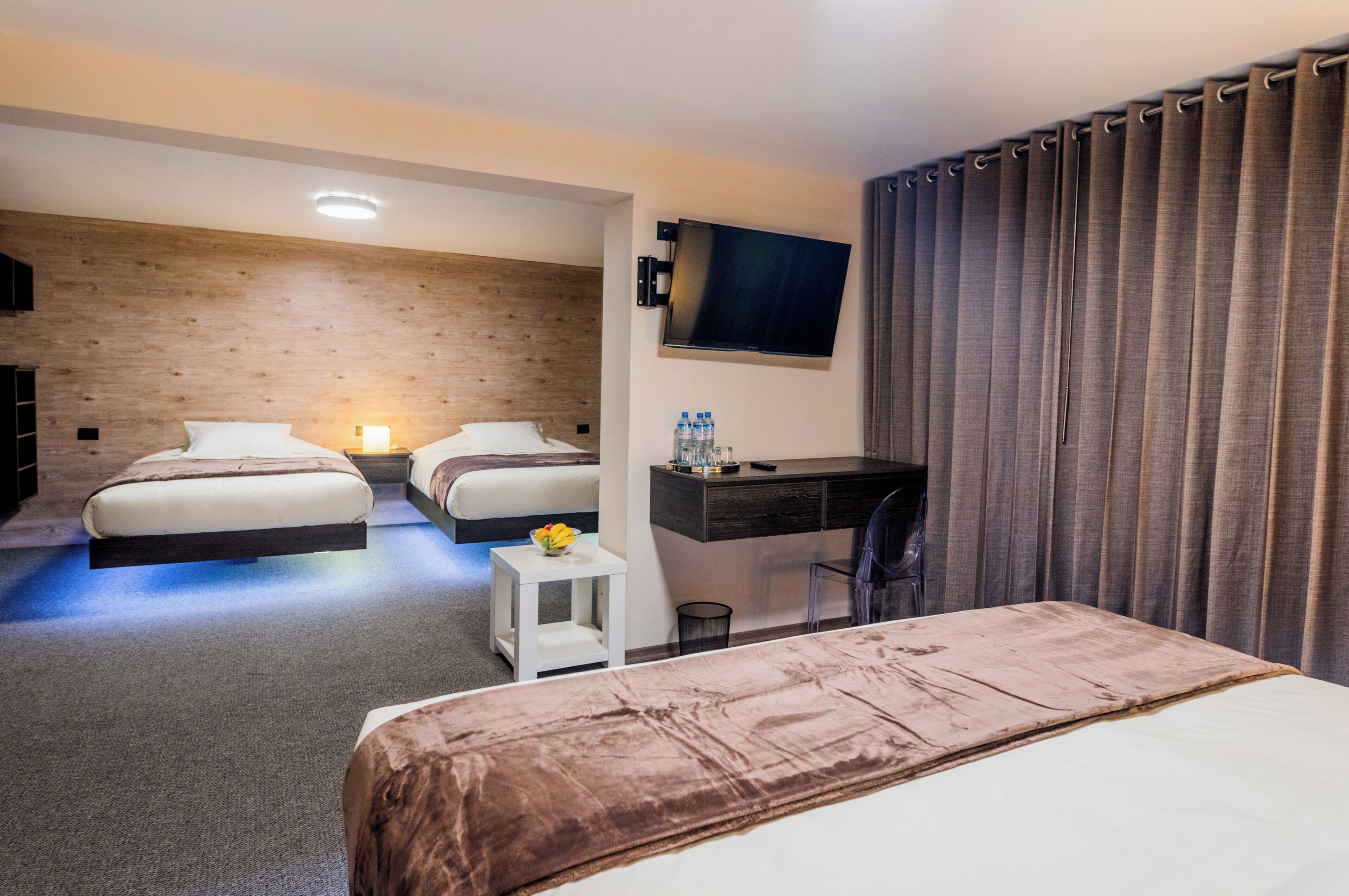 Quarto de hotel com duas camas, uma escrivaninha, uma TV e uma cortina.