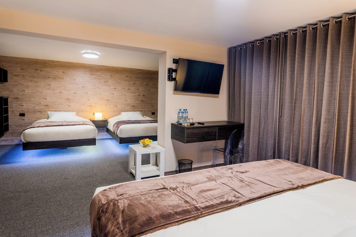Quarto de hotel com duas camas, uma escrivaninha, uma TV e uma cortina.