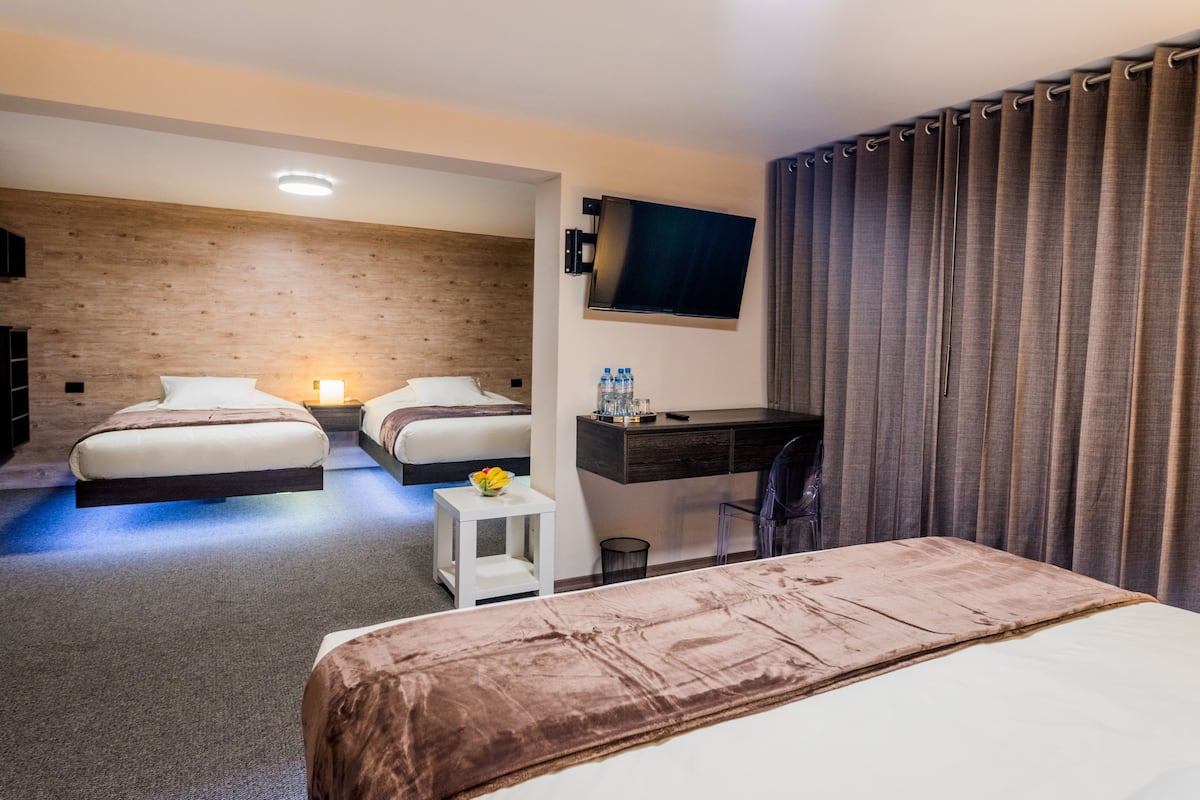 Quarto de hotel com duas camas, uma escrivaninha, uma TV e uma cortina.