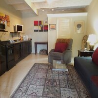 Uma sala de estar com sofá, mesa de centro, tapete, televisão e área de cozinha com armários e micro-ondas.