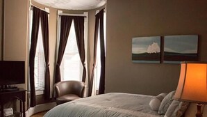 Quarto de hotel com uma cama, uma cadeira, uma televisão e duas pinturas na parede.