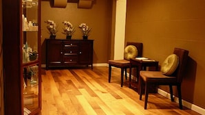 Um quarto com piso de madeira, um armário de madeira escura com gavetas, duas cadeiras com almofadas e um pilar branco alto.