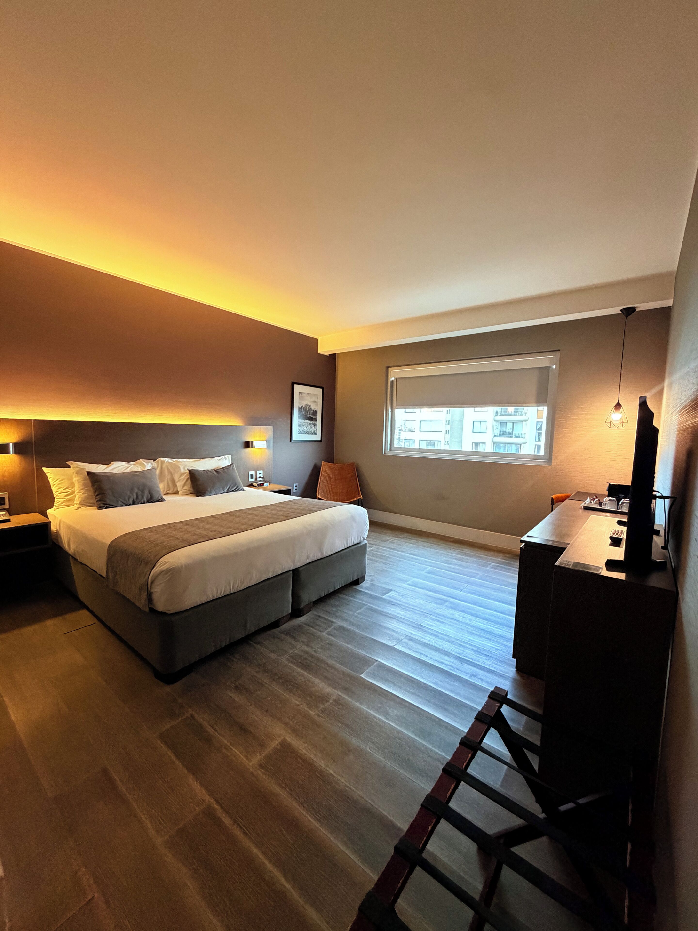 Quarto de hotel moderno com uma cama grande, uma escrivaninha e uma janela com vista para a cidade.