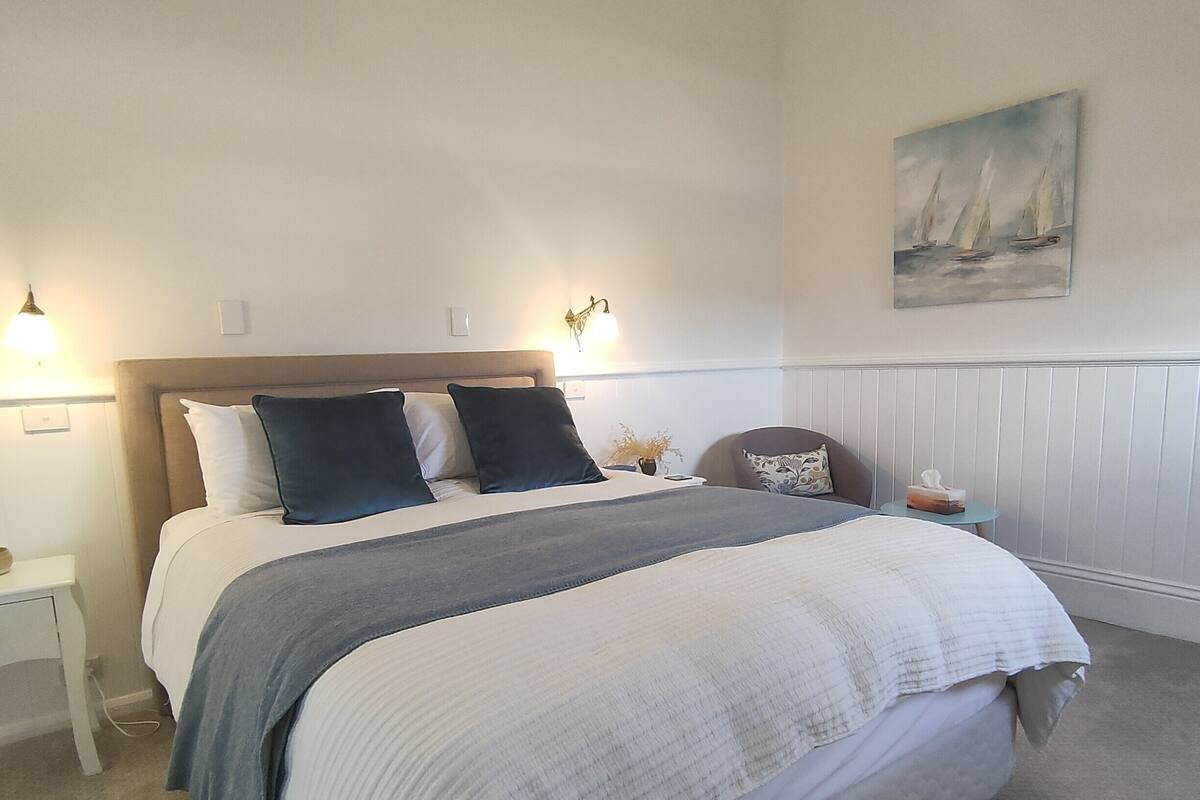 Uma cama bem arrumada com cabeceira, uma mesa de cabeceira com abajur e um quadro pendurado na parede.