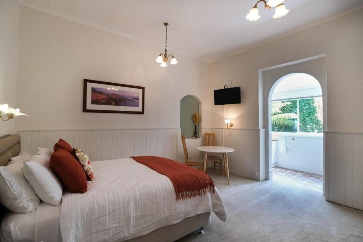 Quarto com cama, uma cadeira, uma mesa, uma televisão e varanda.
