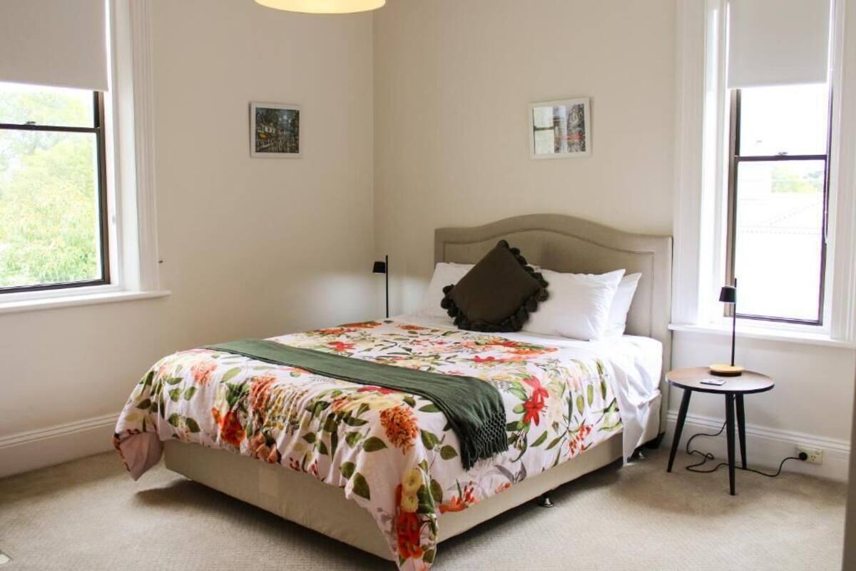Um quarto com uma cama, duas mesas de cabeceira e duas janelas.