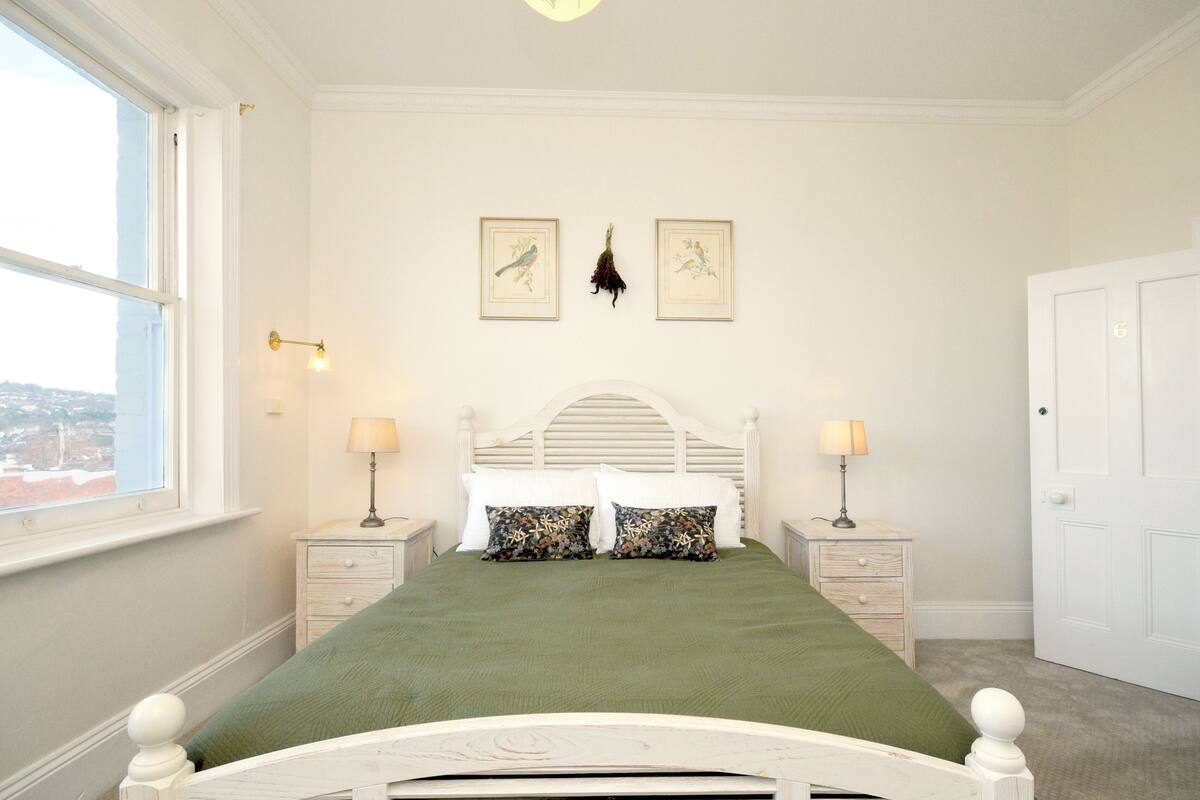 Quarto com uma cama, duas mesas de cabeceira, uma janela e duas molduras na parede.