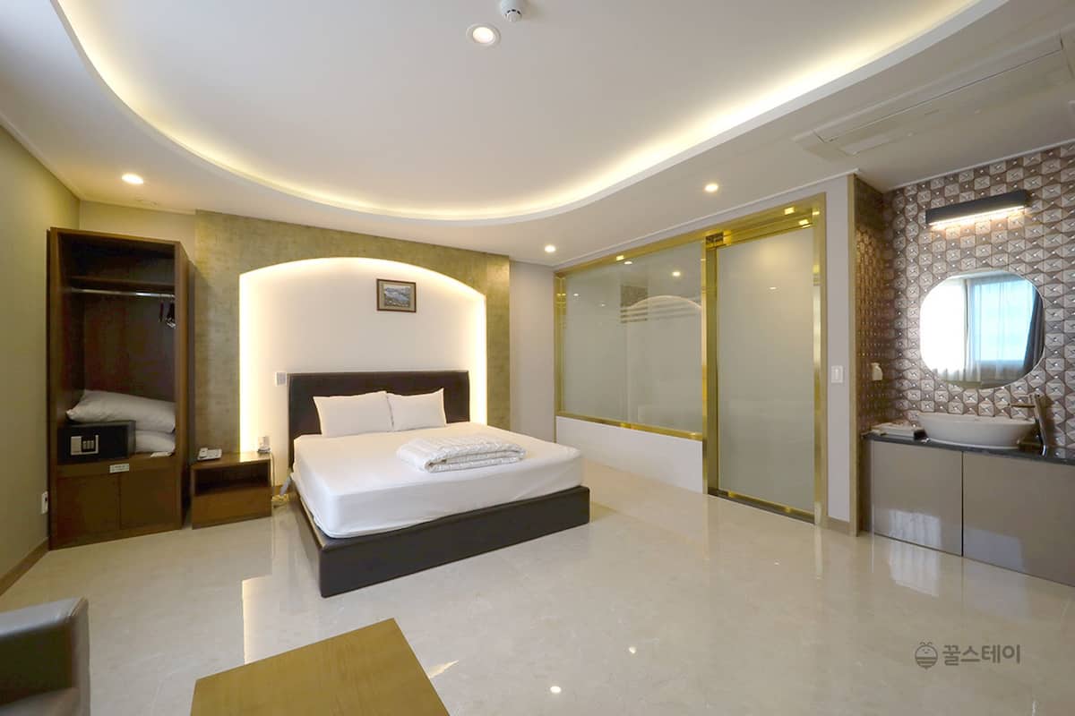 Quarto de hotel moderno com uma cama grande, um closet espaçoso, um banheiro com pia e espelho, e piso lustroso.