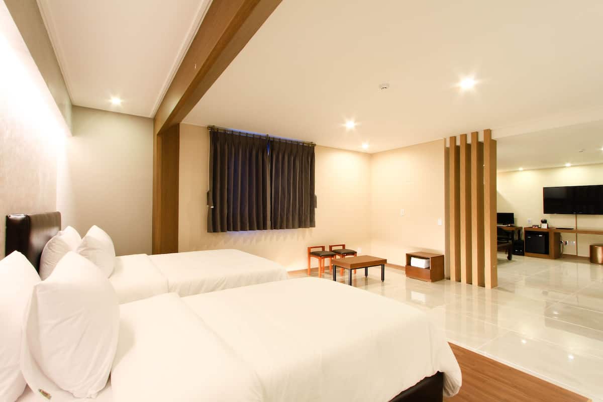 Quarto de hotel com duas camas, uma escrivaninha, uma cadeira, uma televisão e um espelho.