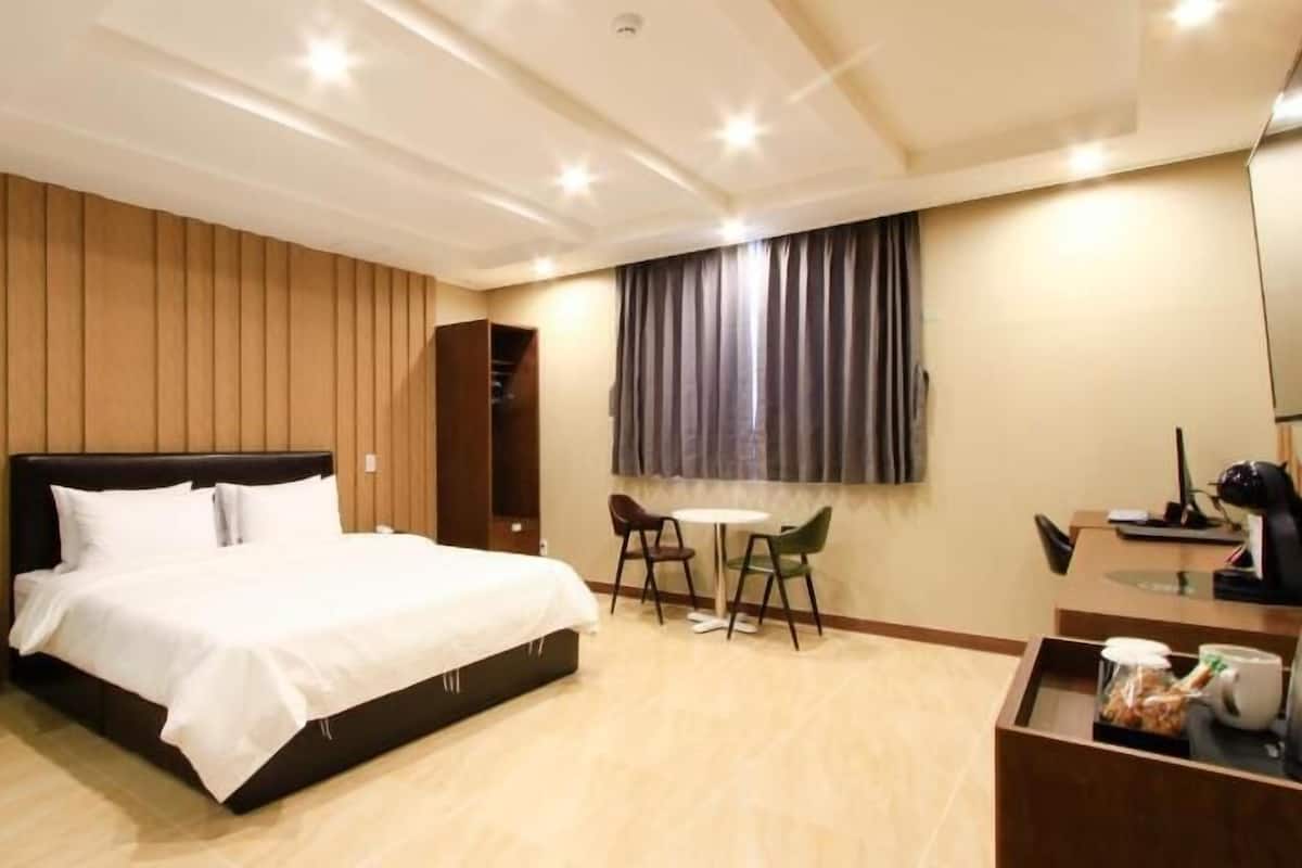 Quarto de hotel com cama, escrivaninha, cadeira, guarda-roupa e máquina de café.
