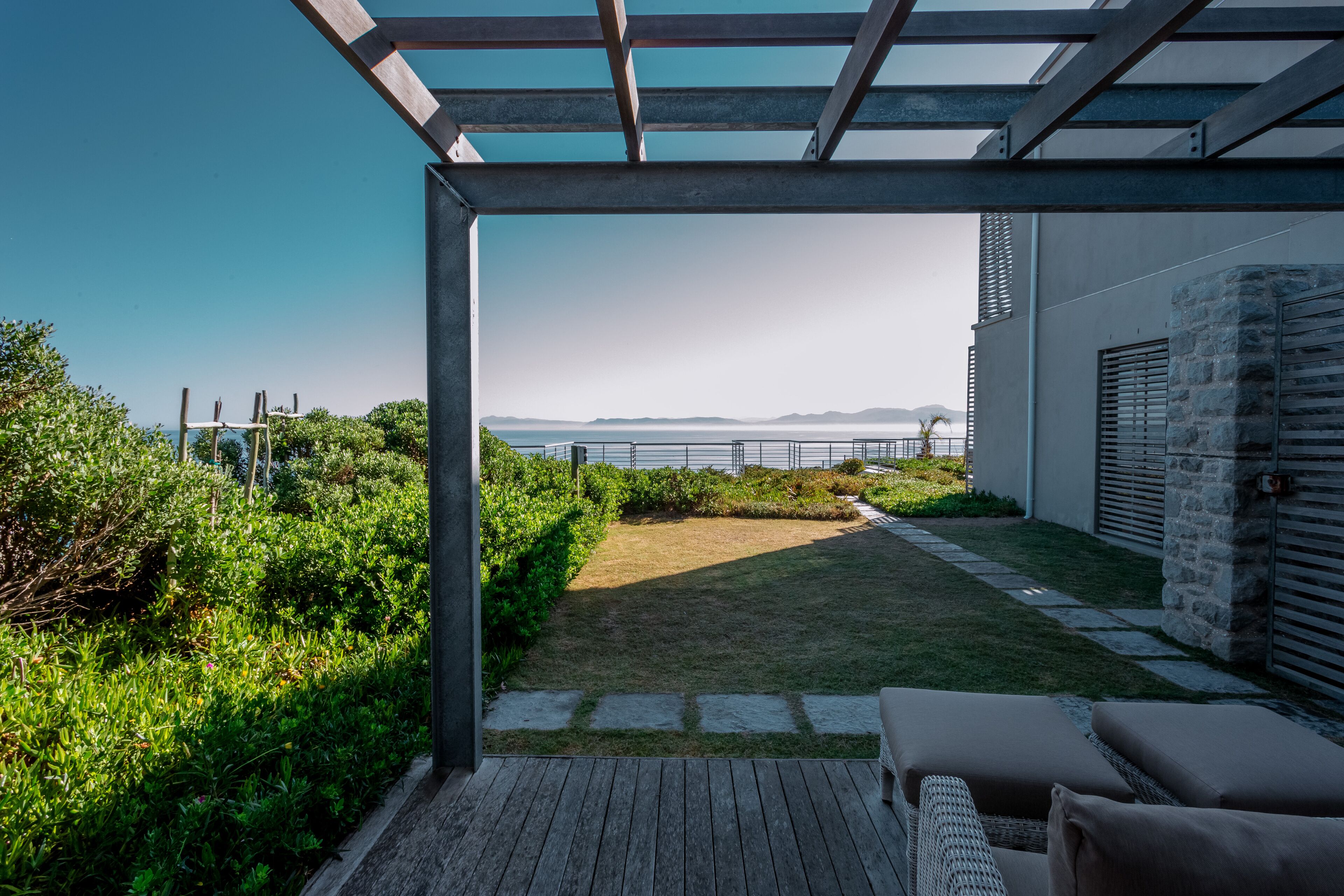 Um alpendre moderno ao ar livre com vista para o mar, um deck de madeira e uma parede de pedra.