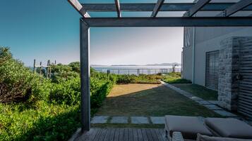 Um alpendre moderno ao ar livre com vista para o mar, um deck de madeira e uma parede de pedra.