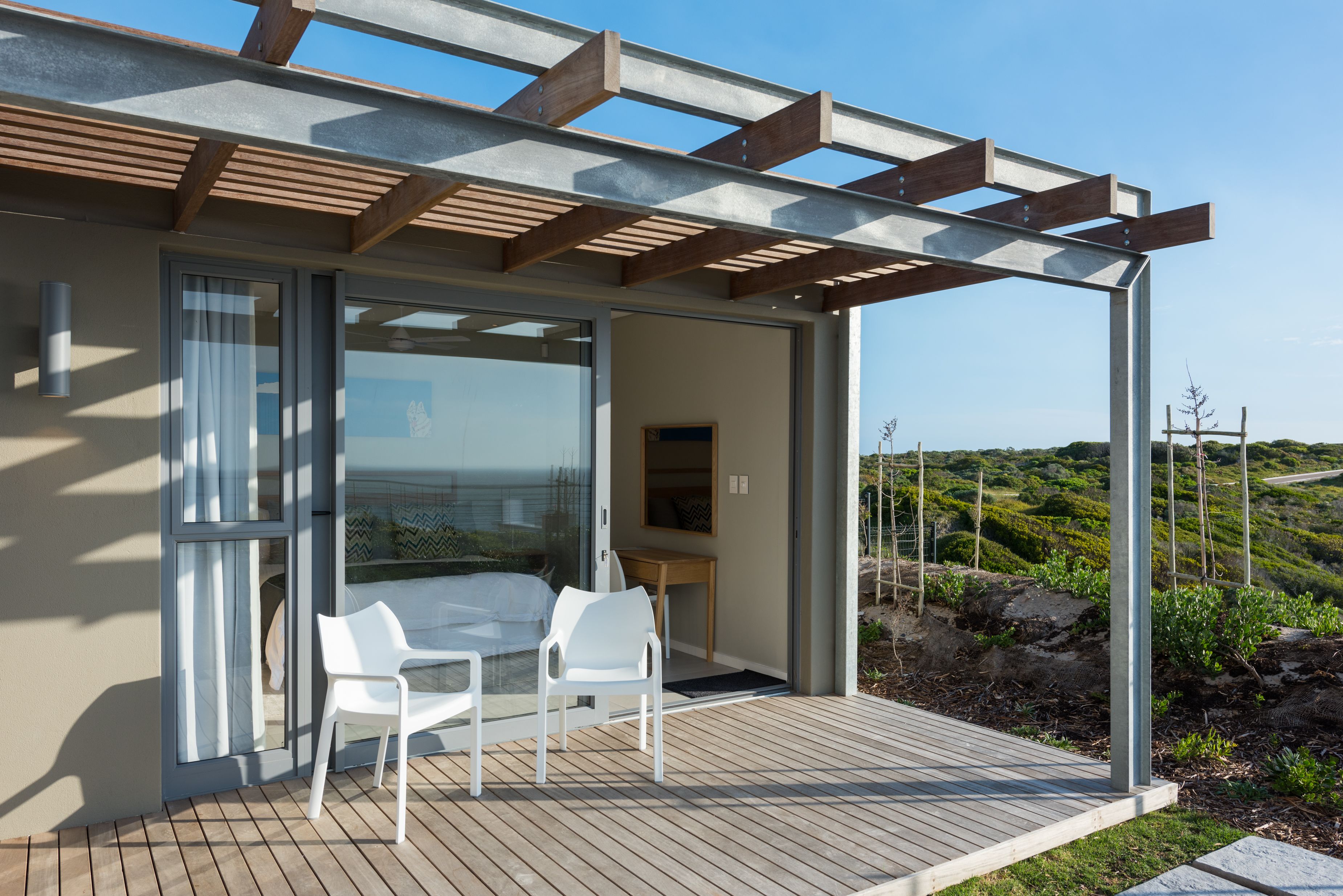 Um pátio moderno ao ar livre com porta de vidro que dá para um quarto, um deck de madeira e vista para a paisagem.