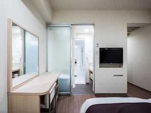 Quarto de hotel com cama, escrivaninha, espelho, televisão e área de duche.