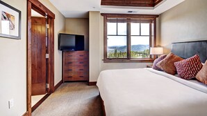 Quarto com cama, televisão, janela com vista para as montanhas e porta de madeira.