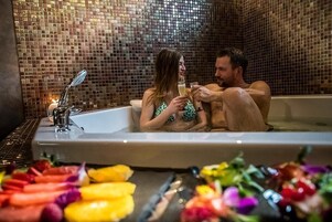Um casal em banheira, com parede em mosaico e flores ao redor.