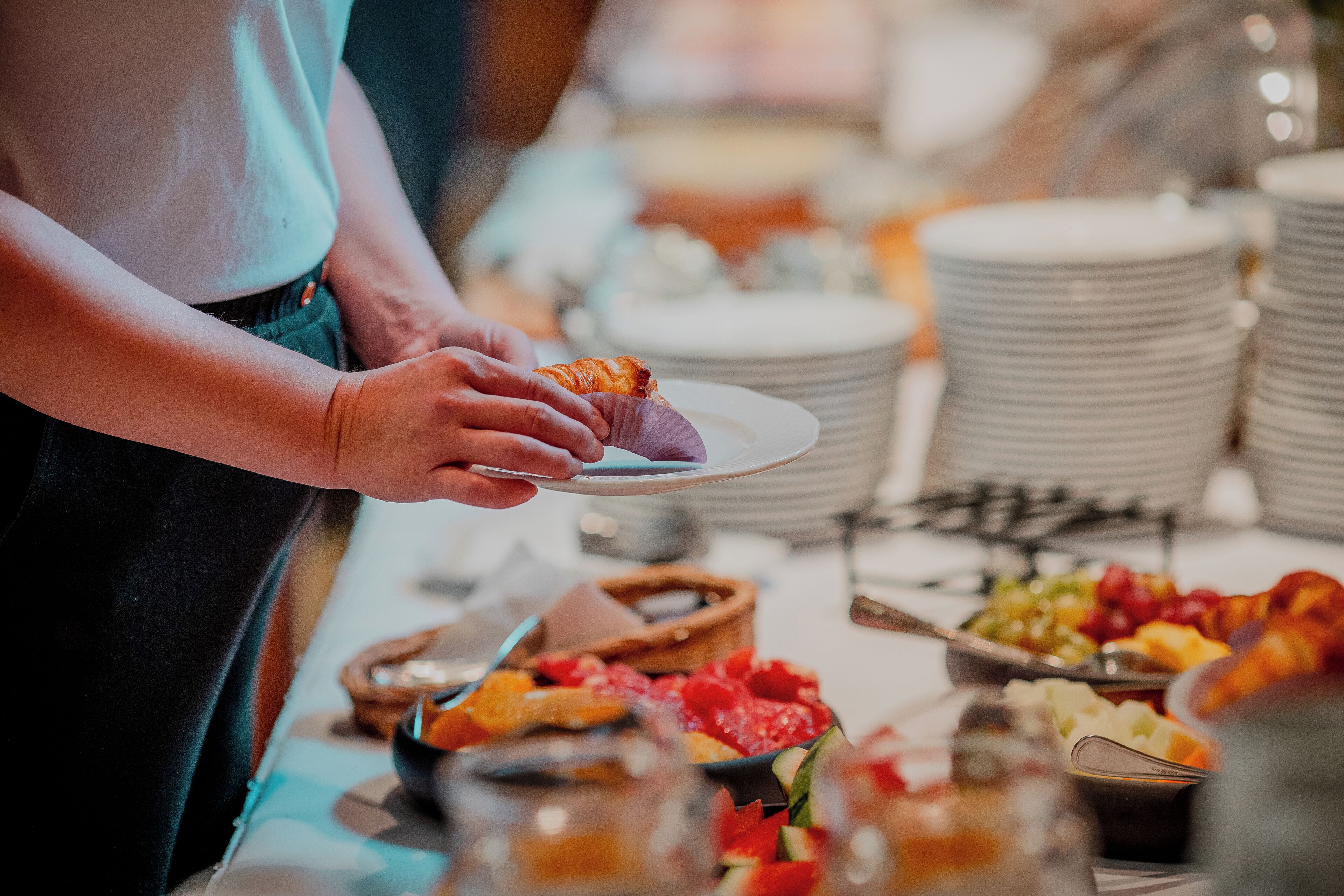 Disposição de buffet com diversos alimentos e pratos empilhados.