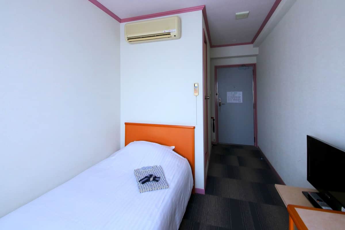 Quarto de hotel com uma cama de solteiro, televisão de tela plana e uma pequena escrivaninha.