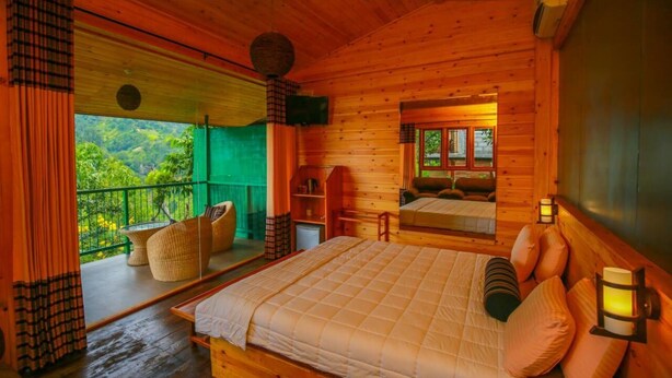 Quarto de cabana de madeira com uma cama, um pequeno espaço de estar e uma varanda com vista para o verde.