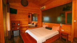 Quarto de cabana de madeira com cama, mesa de cabeceira e pequena escrivaninha com cadeira.