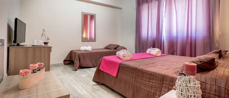 Quarto de hotel com duas camas, uma televisão, um espelho e uma mesinha com um vaso.