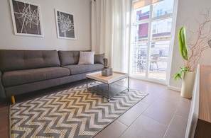 Uma sala de estar moderna com um sofá cinzento, uma mesa de centro e um tapete estampado.