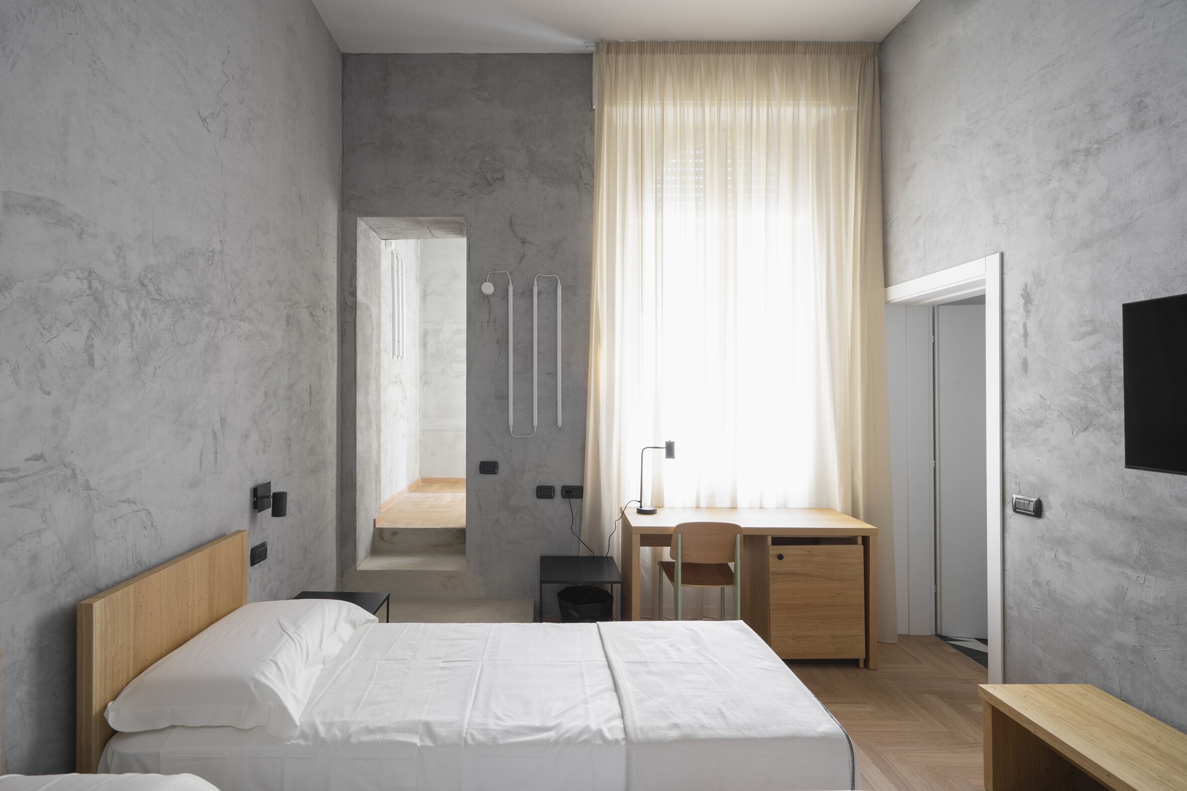 Quarto moderno com cama, escrivaninha e cadeira, uma porta e uma janela com cortinas.