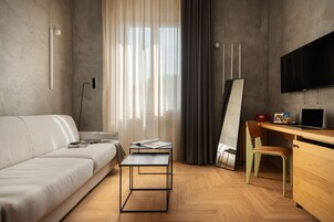Uma sala de estar moderna com sofá, mesinha, escrivaninha, cadeira, televisão e uma janela grande com cortinas.