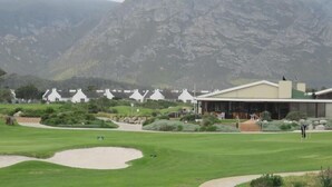 Um campo de golfe com um clube, edifícios com telhados brancos e um cenário montanhoso.