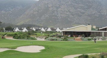 Um campo de golfe com um clube, edifícios com telhados brancos e um cenário montanhoso.