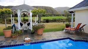 Piscina com um gazebo branco, plantas em vasos e móveis de exterior.