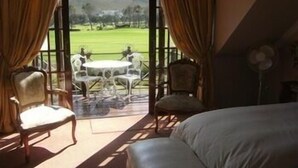 Quarto com cama grande, vista para um campo de golfe e área de refeições com cadeiras e mesa.