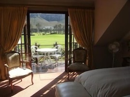Quarto com cama grande, vista para um campo de golfe e área de refeições com cadeiras e mesa.