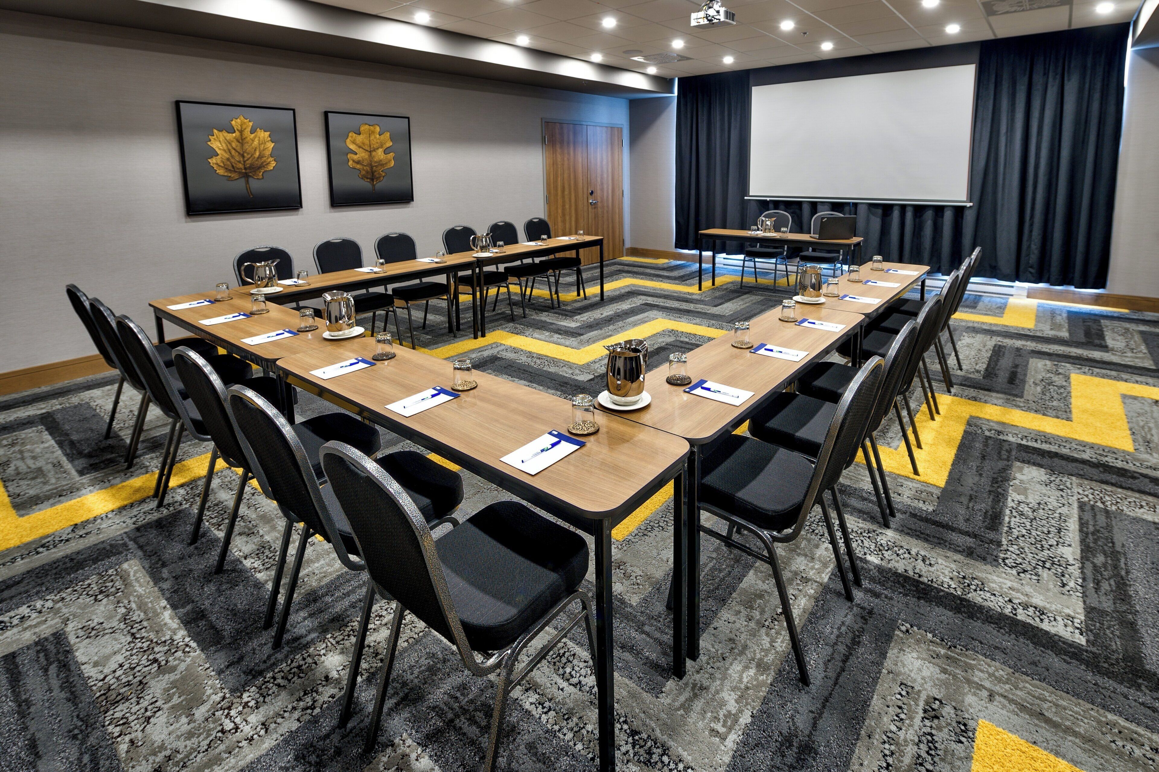 Uma sala de conferências com uma mesa comprida, cadeiras, tela de projetor e tela de apresentação.
