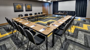 Uma sala de conferências com uma mesa comprida, cadeiras, tela de projetor e tela de apresentação.