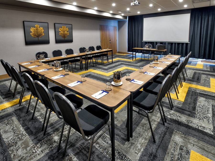 Uma sala de conferências com uma mesa comprida, cadeiras, tela de projetor e tela de apresentação.