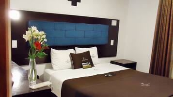 Quarto de hotel com uma cama, mesa de cabeceira, vaso com flores e um objeto decorativo na parede.