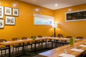 Uma sala de conferência com uma mesa comprida, cadeiras, quadros nas paredes, uma janela e um abajur.